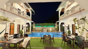 Área de piscina externa com mesas e cadeiras, cercada por edifícios brancos com varandas.