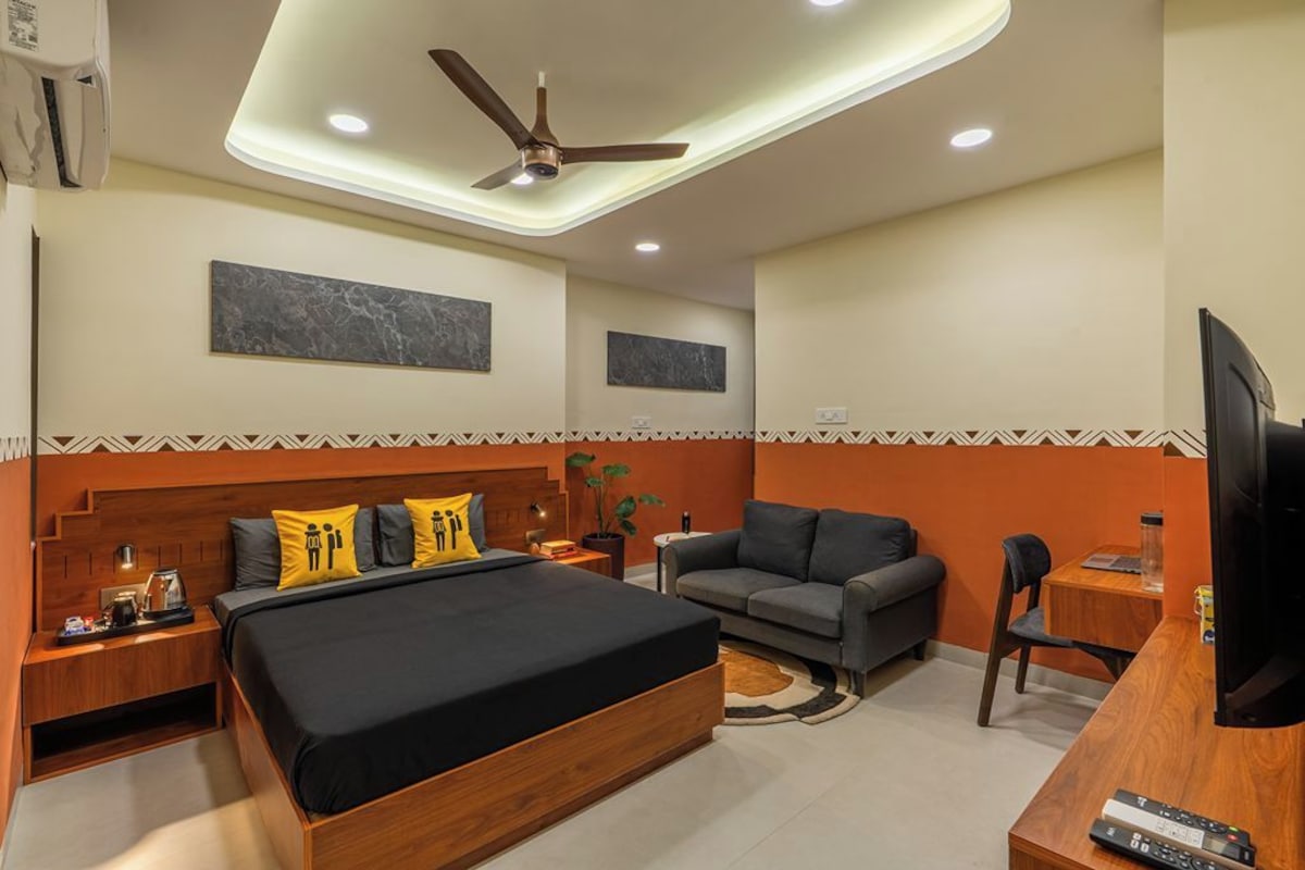 Quarto de hotel com cama, sofá, televisão e ventoinha no teto.