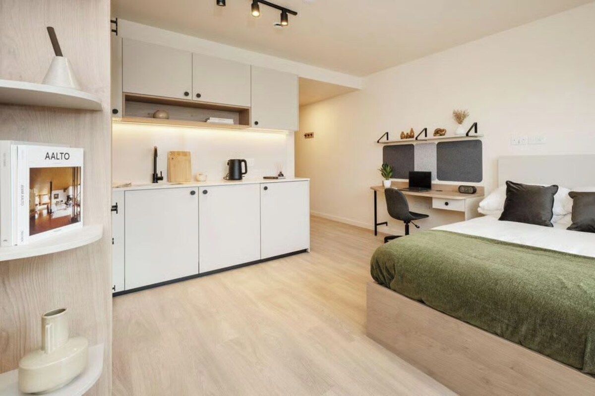 Quarto moderno com cama, escrivaninha e área de kitchenette.
