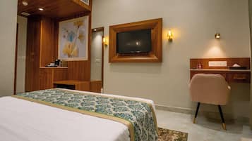 Quarto de hotel com cama, escrivaninha, cadeira, televisão e luminária na parede.