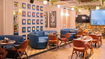 Restaurante com assentos azuis, piso em padrão herringbone e parede decorada com pratos redondos.