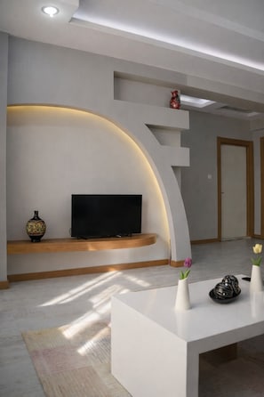 Uma sala de estar moderna com uma TV de tela plana em uma estante embutida, um vaso com flores e uma tigela decorativa em um console branco.