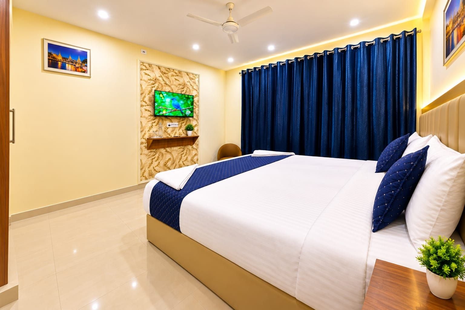 Quarto de hotel com cama, televisão, ventoinha no teto e janela com cortinas.