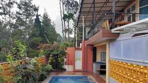 Área de piscina com deck de madeira, espaço coberto para sentar e vista para área arborizada.
