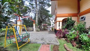 Um parquinho com balanços e escorrega, um caminho pavimentado e um edifício com entrada coberta.