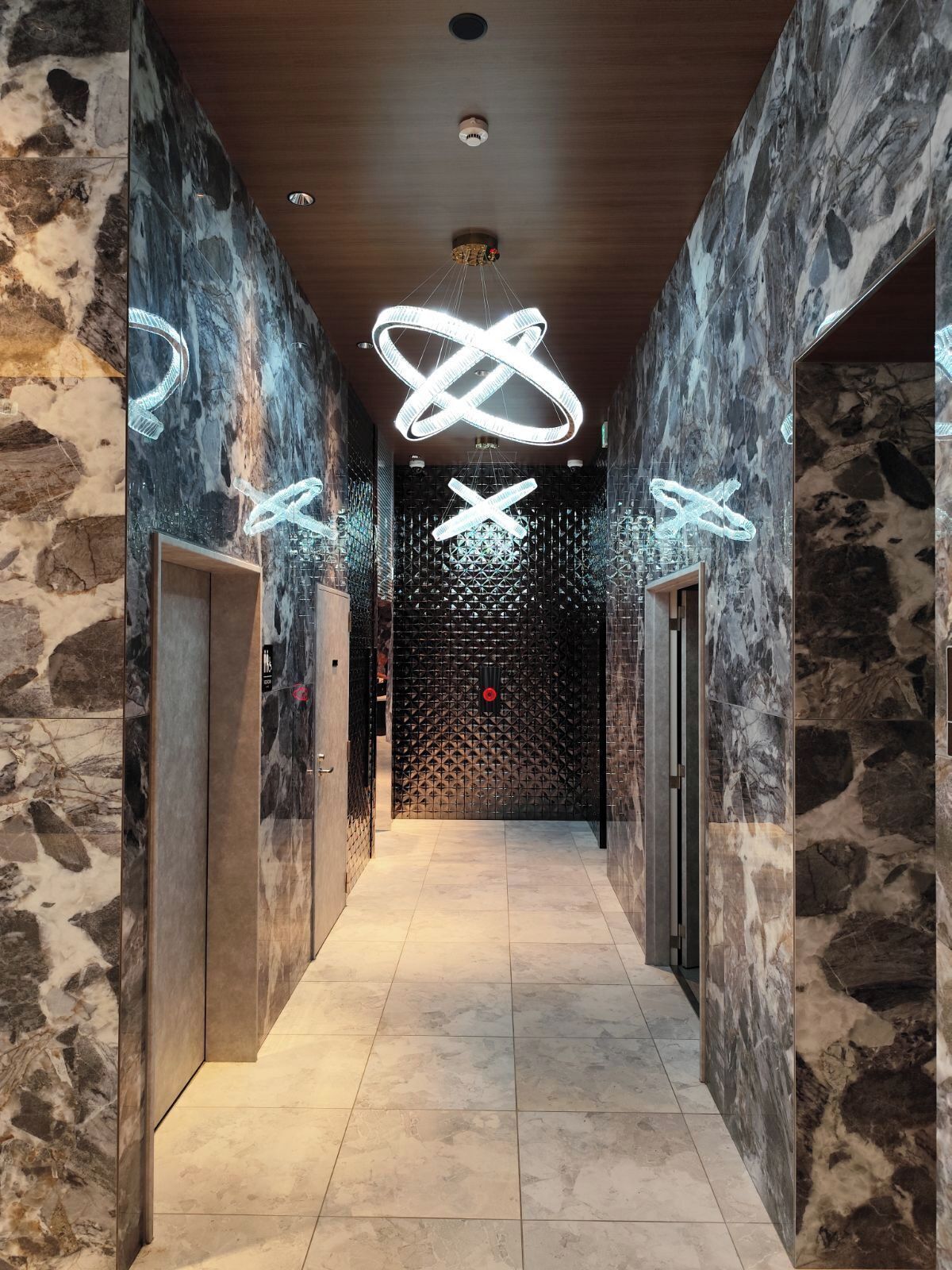Corredor com paredes de mármore e luminária de design geométrico.