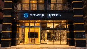 Exterior do Tower Hotel com fachada moderna, ampla entrada de vidro e placa de hotel bem visível.