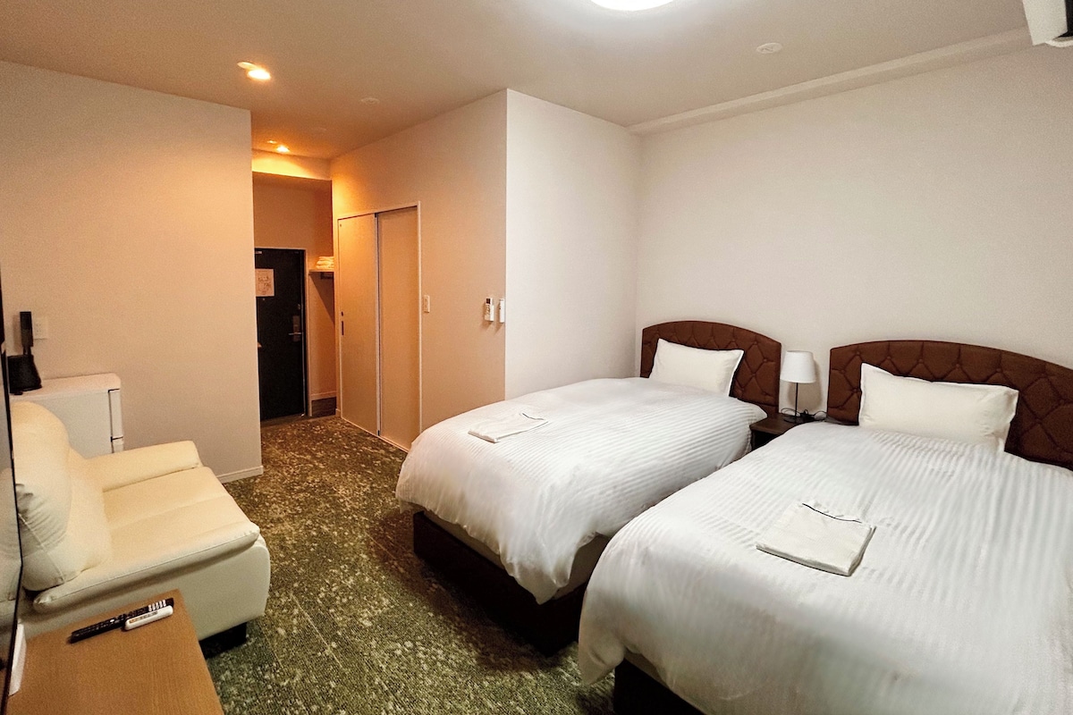 Quarto de hotel com duas camas, um sofá, uma escrivaninha e um banheiro.