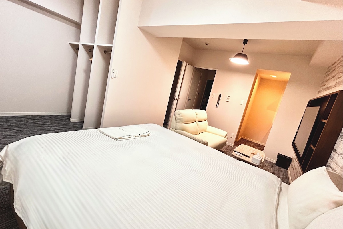 Quarto de hotel com uma cama grande, uma cadeira, uma escrivaninha e um guarda-roupa.