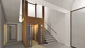 Interior moderno com escada, elevador de vidro e parede lisa.