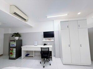 Um espaço de escritório moderno com uma mesa branca, cadeira de escritório preta, TV de tela plana, guarda-roupa branco e um ar-condicionado.