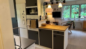 Cozinha compacta com forno embutido, bancada de madeira e espaço de jantar com uma cadeira.