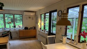 Cozinha moderna com armários de madeira, uma mesa de jantar e cadeiras. Janelas oferecem vista para o verde lá fora.