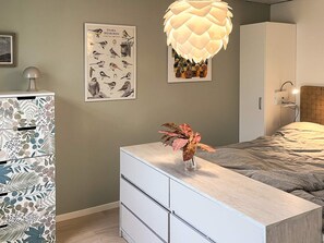 Quarto com cama, cômoda, luminária na parede e pôster de aves.