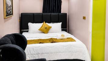 Quarto de hotel com cama, cadeiras estofadas pretas, uma mesa redonda preta, ar condicionado fixado na parede e uma porta verde vibrante.