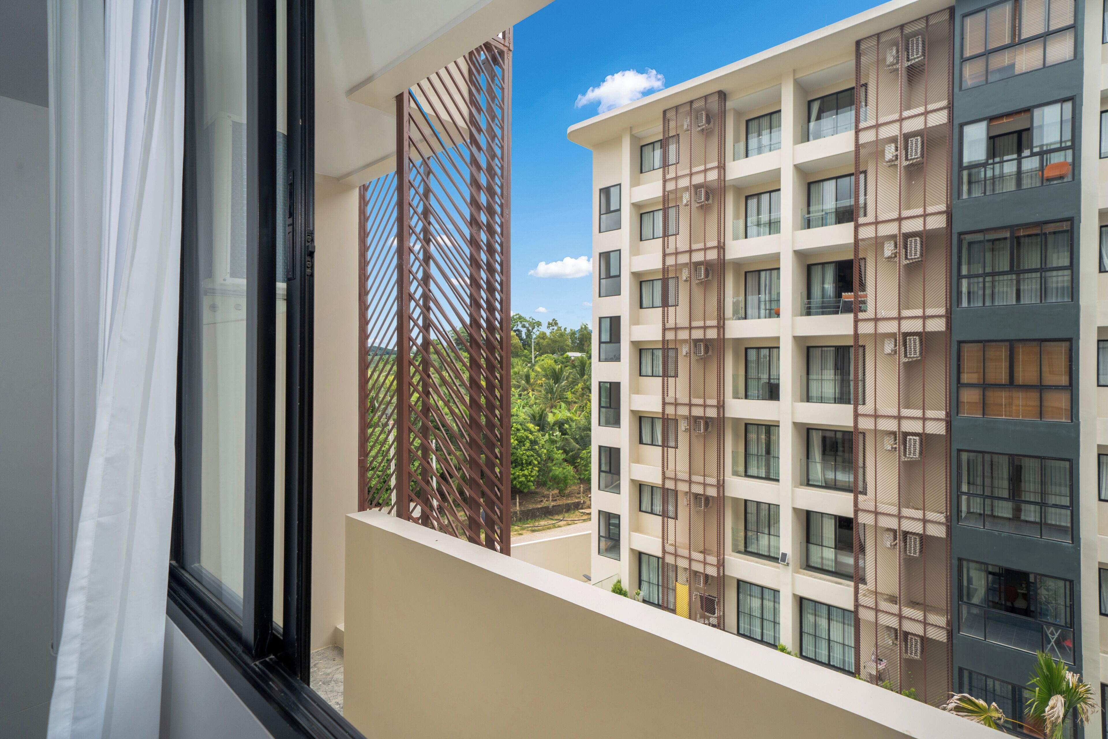 Vista de varanda com divisória metálica, com vista para um edifício com várias andares, varandas e aparelhos de ar condicionado.
