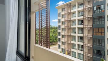 Vista de varanda com divisória metálica, com vista para um edifício com várias andares, varandas e aparelhos de ar condicionado.