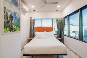 Quarto de hotel com cama, vista da cidade, ventoinha no teto e ar condicionado.