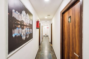 Corredor de hotel com placa de saída de incêndio, extintor e porta com número.