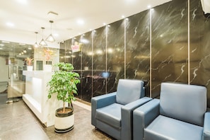 Uma área de recepção de hotel com parede de mármore, balcão de atendimento e assentos azuis.
