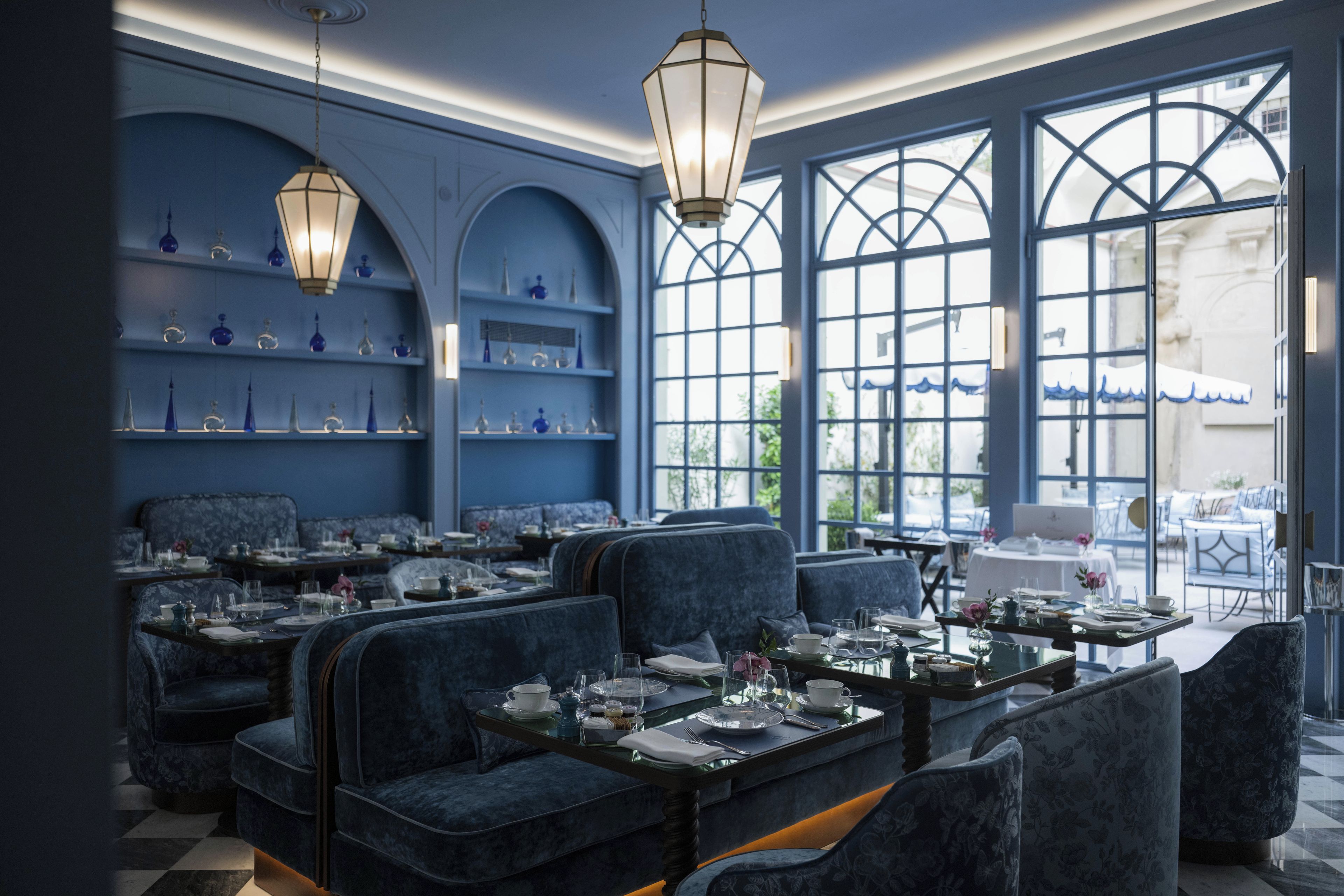 Restaurante com paredes azuis, janelas em arco e assentos estofados em azul.