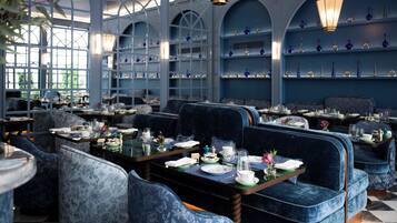 Restaurante com assentos estofados em azul, mesas dispostas com pratos, copos e talheres, e teto decorativo com luminárias pendentes.