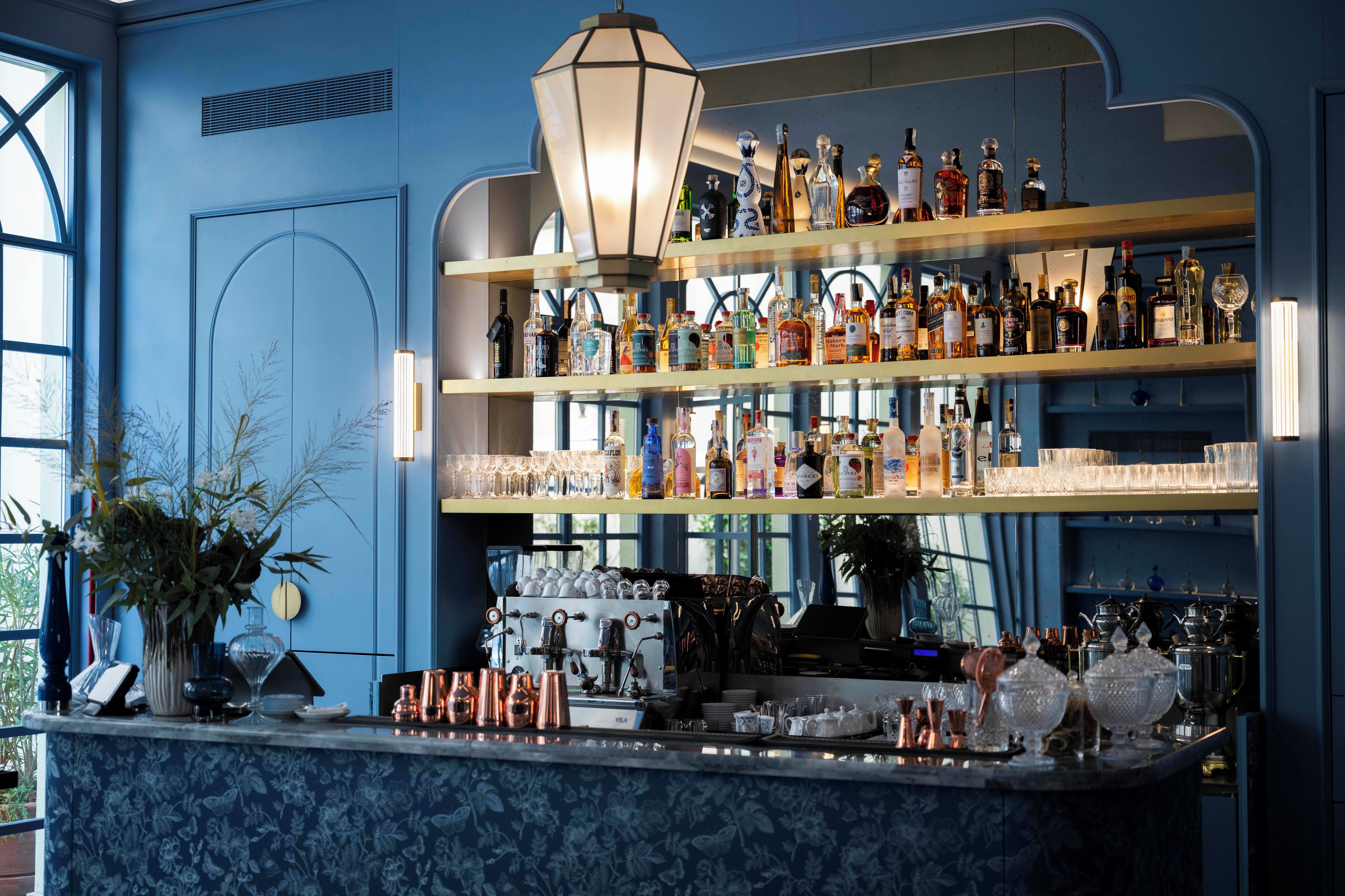 Uma área de bar com prateleiras cheias de garrafas de bebidas, uma máquina de café e um vaso decorativo.
