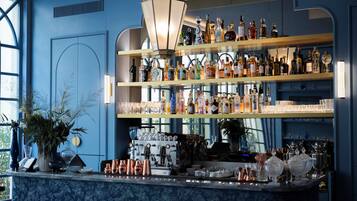 Uma área de bar com prateleiras cheias de garrafas de bebidas, uma máquina de café e um vaso decorativo.