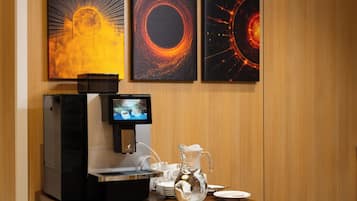 Máquina de café com visor digital, jarra de vidro e prato com xícara sobre bancada de madeira.