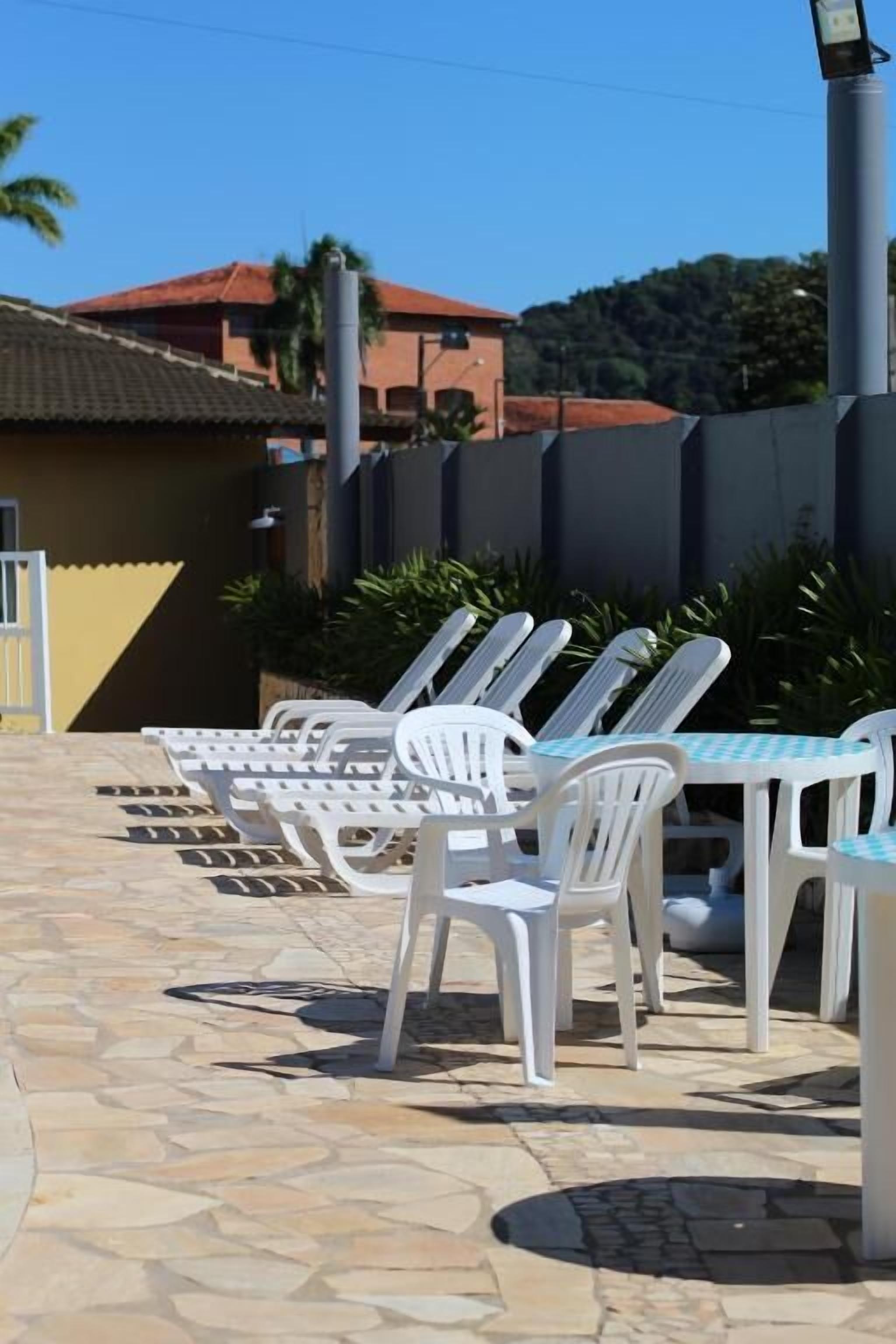 Mobiliário de exterior com cadeiras e mesas de plástico branco, dispostas num terraço de pedra.