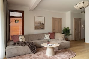 Uma sala de estar com sofá, mesa de centro, planta e um quadro na parede.