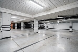 Estacionamento subterrâneo com pilares de concreto, um carro estacionado em uma das vagas e iluminação suspensa.