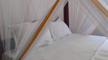Cama com dossel, almofadas e cabeceira de madeira.