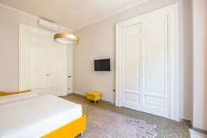 Quarto com cama, televisão, um pequeno banquinho e dois armários.