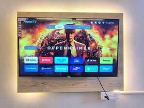 Uma tela de televisão exibindo a interface Android TV com diversos ícones de aplicativos e o título 'OPPENHEIMER' em destaque.