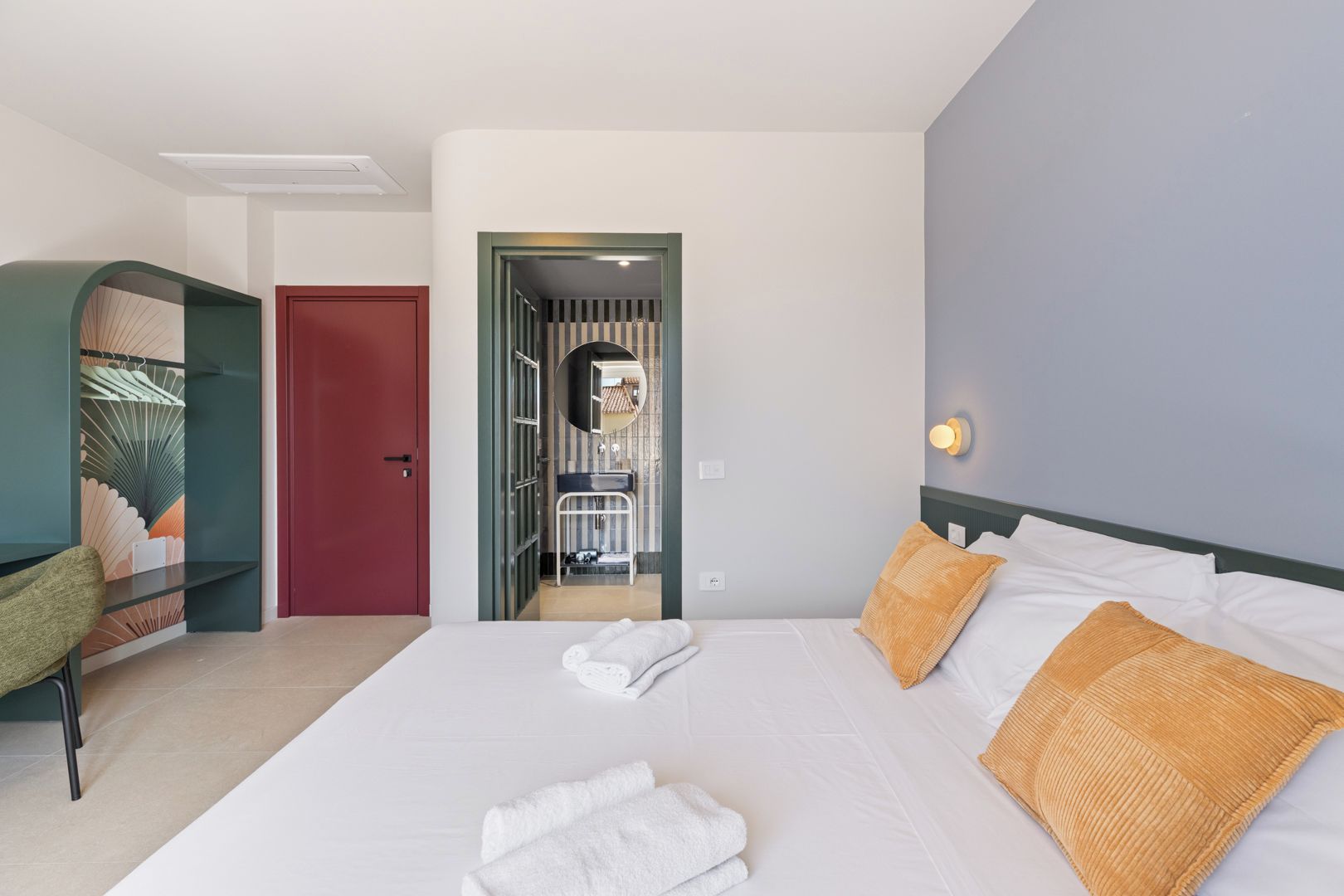Quarto de hotel com cama, escrivaninha e banheiro visível por uma porta aberta.