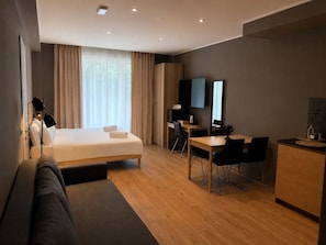 Quarto de hotel moderno com cama, escrivaninha, sofá e televisão.