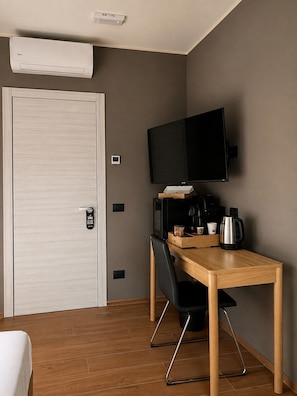 Quarto de hotel com escrivaninha de madeira, cadeiras pretas, televisão e máquina de café.