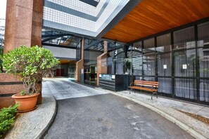 Entrada de um edifício moderno com um banco, uma placa indicando 'Hotel Parking' e um vaso de planta.