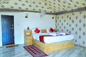 Quarto com cama, mesa de cabeceira, ventilador na parede e papel de parede estampado.
