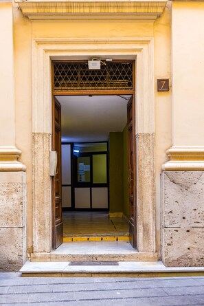 Entrada de um edifício com portão de metal, placa de número e porta para o interior.