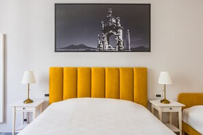 Quarto de hotel com uma cama grande, duas mesas de cabeceira e um quadro emoldurado na parede.