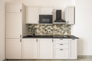 Cozinha com armários brancos, micro-ondas preto e painel de parede decorado.
