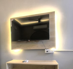 Televisão de tela plana presa na parede com uma prateleira de madeira abaixo.