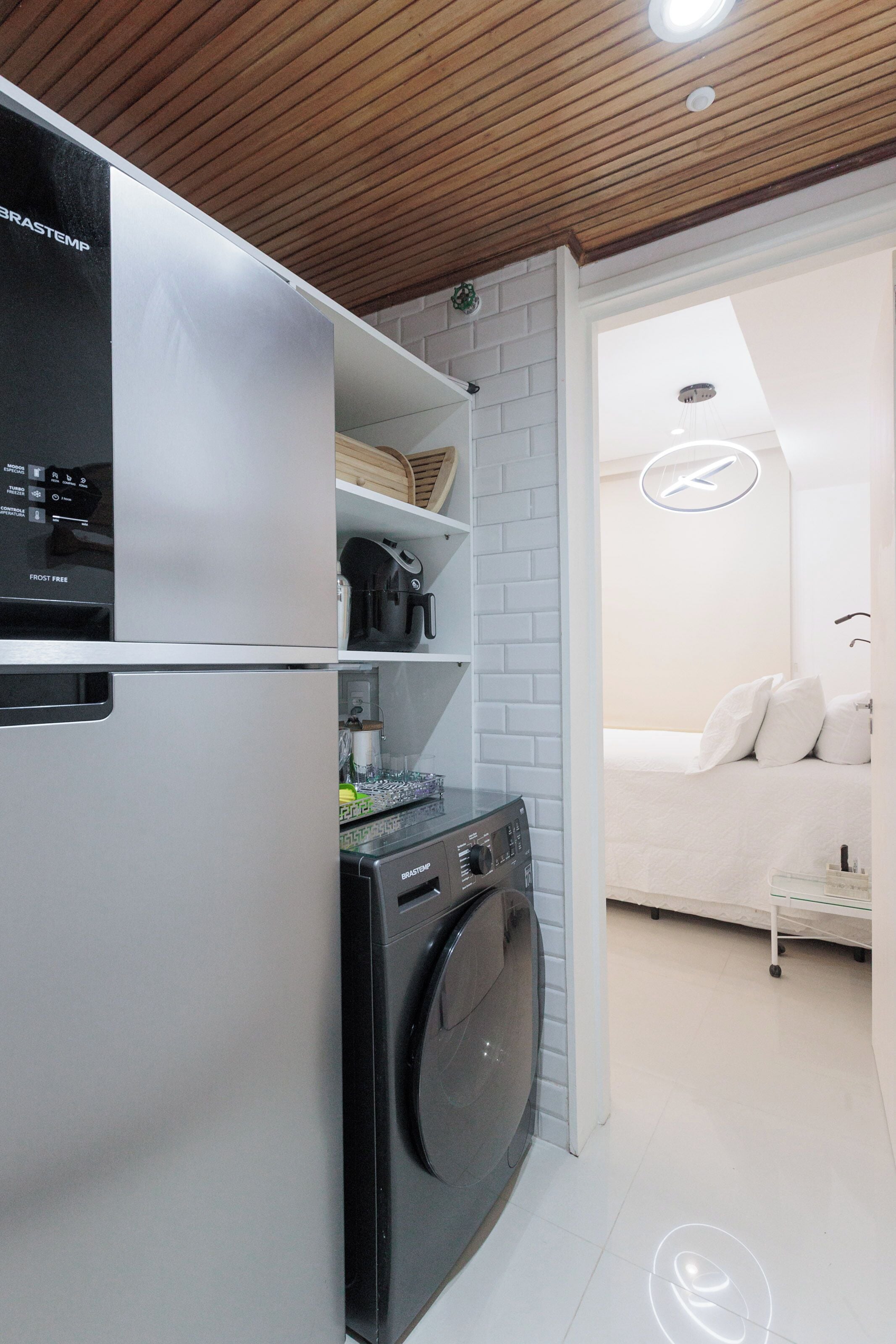 Cozinha compacta com máquina de lavar embutida, geladeira e pequena área de refeições com mesa e cadeiras brancas.