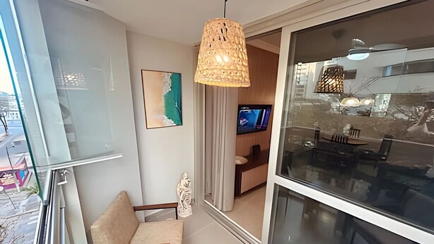Uma sala de estar moderna com divisória de vidro, luminária pendente trançada, televisão e sofá.