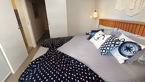 Quarto com uma cama, ar-condicionado fixado na parede, um enfeite de macramé e uma porta que dá para outro cômodo.