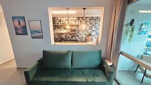 Uma sala de estar moderna com um sofá verde, uma área de jantar com divisória de vidro e obras de arte nas paredes.