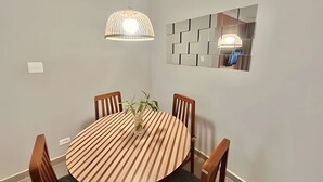 Uma sala de jantar com mesa redonda, cadeiras de madeira, luminária pendente e espelho fixado na parede.