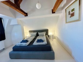 Quarto com cama, mesas de cabeceira, luminária pendente e quadro na parede.